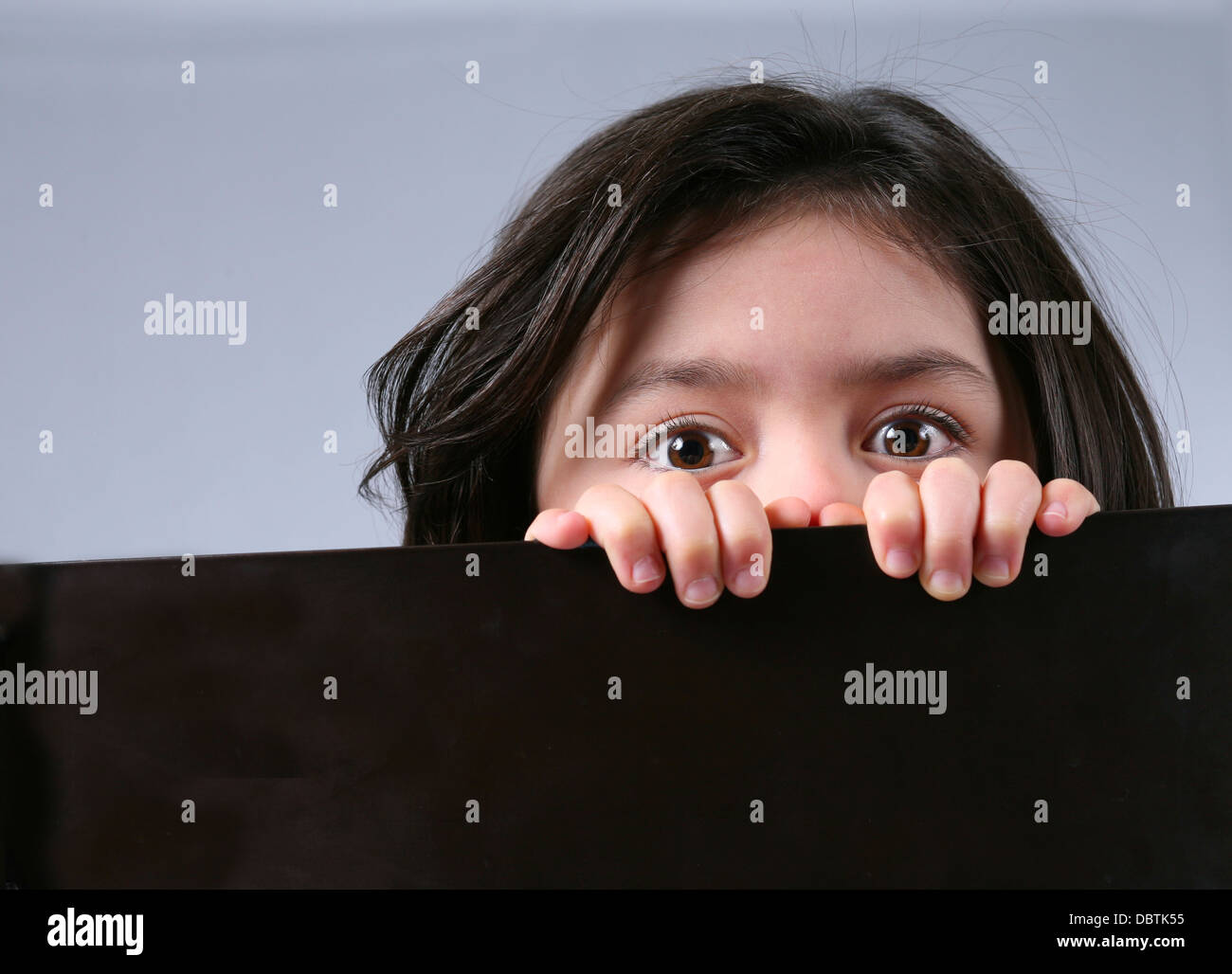 serious little brunette girl peeking over edge Stock Photo - Alamy