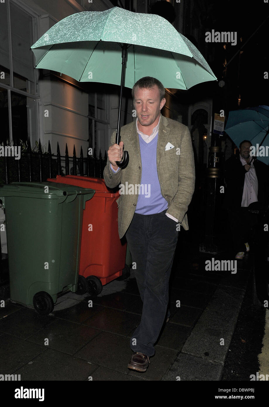 Guy Ritchie walking through Mayfair holding a large umbrella to protect ...