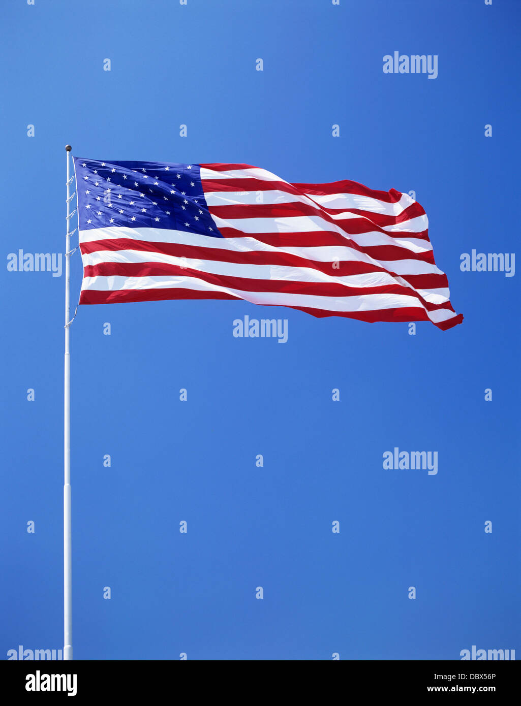 U.S. FLAG FLYING UNFURLED IN THE BREEZE AGAINST CLOUDLESS BLUE SKY ...