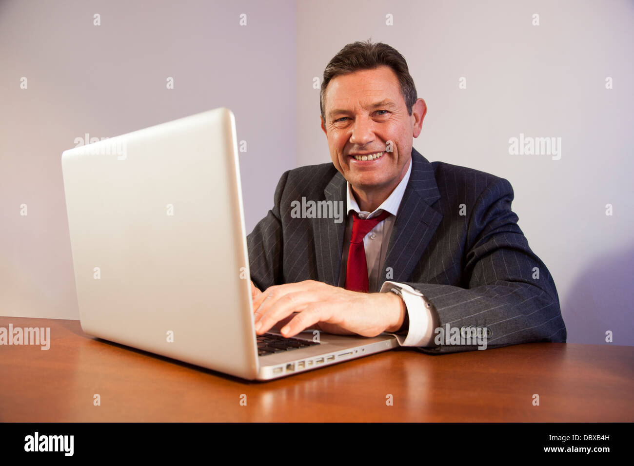 Business man at a desk using a laptop computer, looking at camera ...