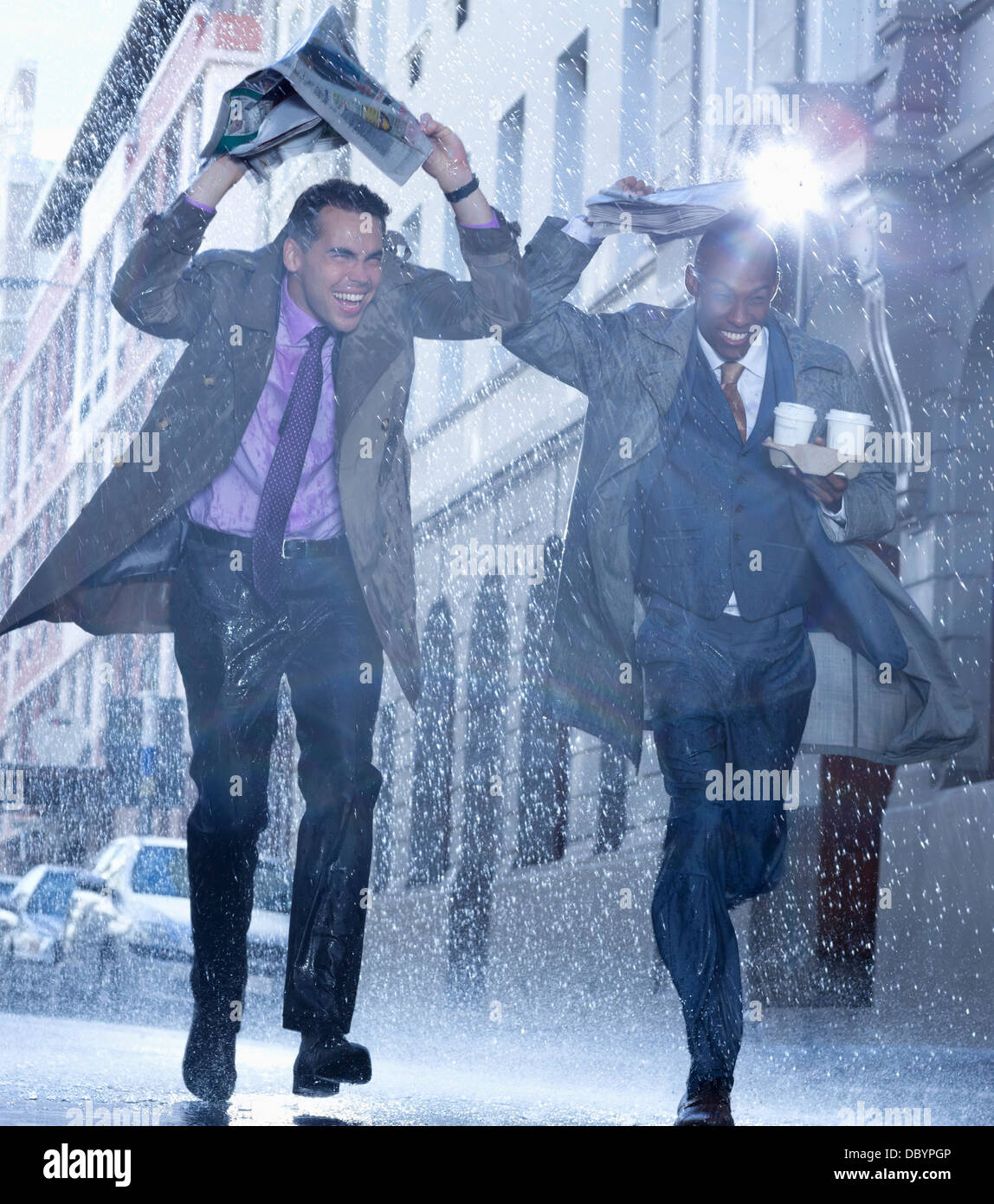 Businessmen carrying coffee and covering heads with newspaper in rain ...
