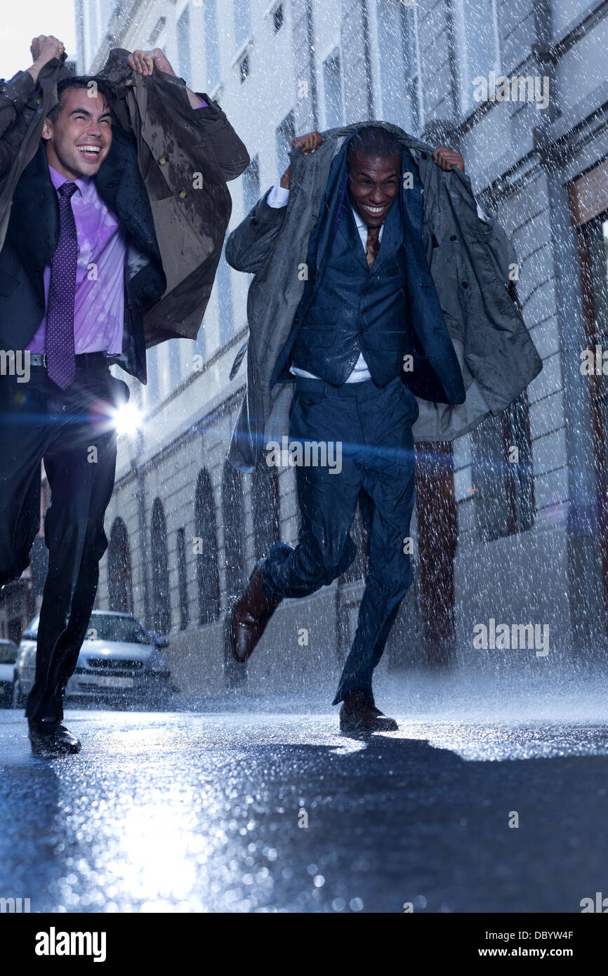 Happy businessmen covering heads with coats in rainy street Stock Photo ...