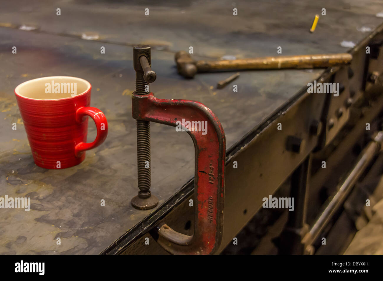 Engineers bench with empty cup and G clamp hammer and punch Stock Photo ...