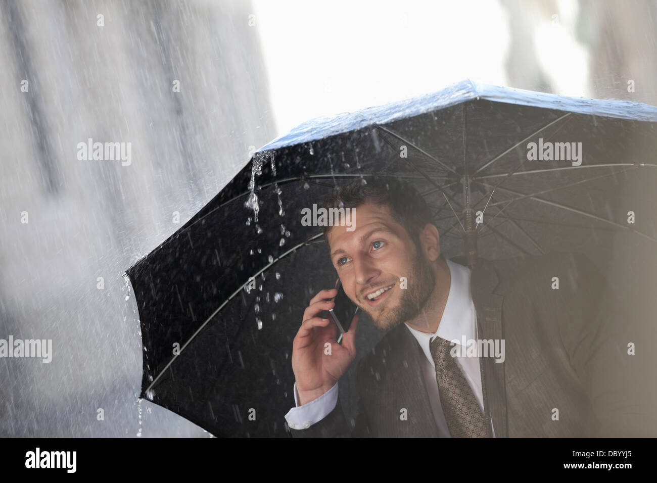 Businessman talking on cell phone under umbrella in rain Stock Photo ...