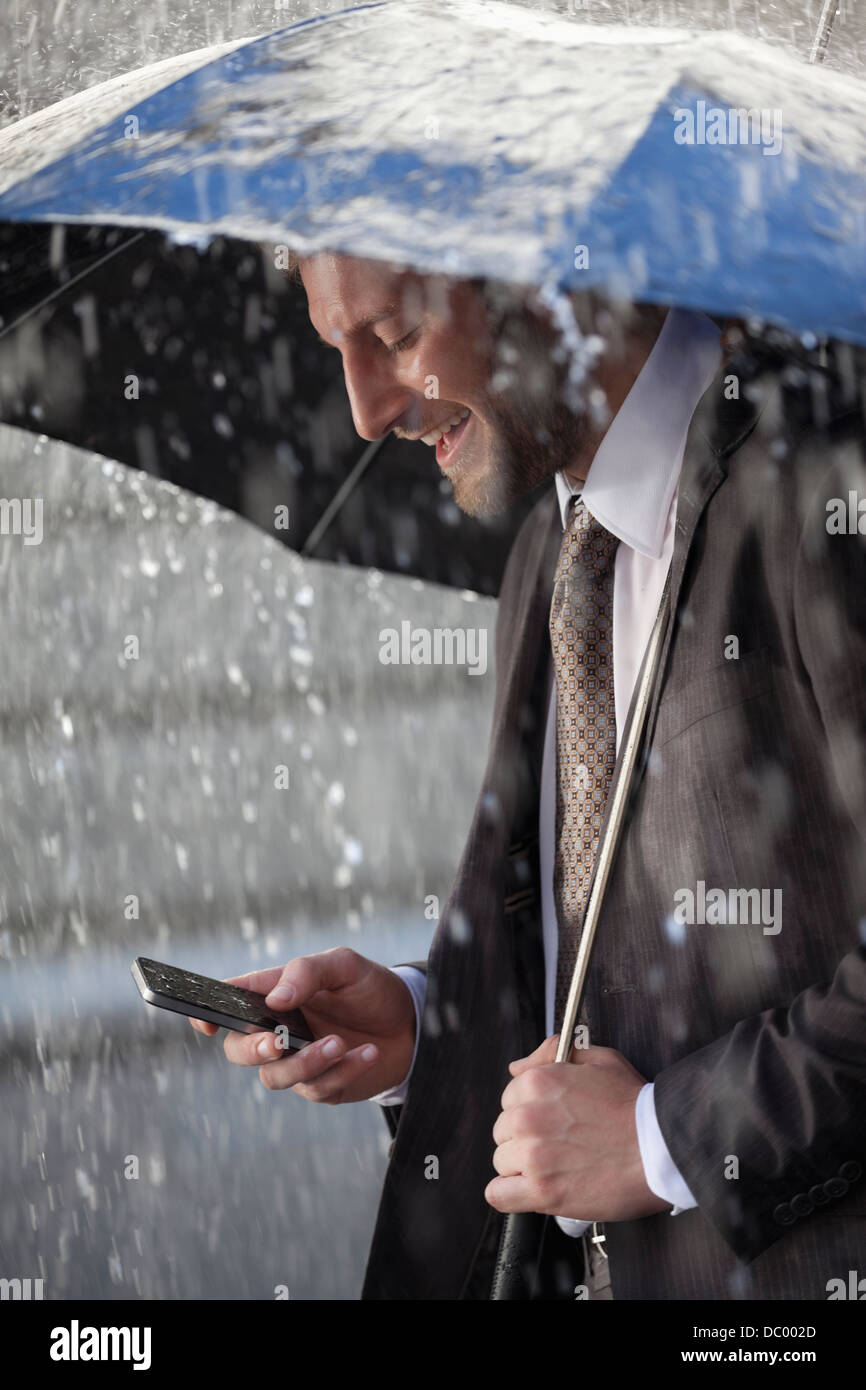 Businessman text messaging on cell phone under umbrella in rain Stock ...