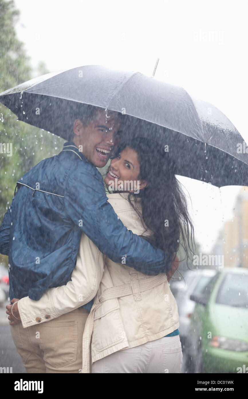 Portrait of happy couple hugging under umbrella in rain Stock Photo - Alamy