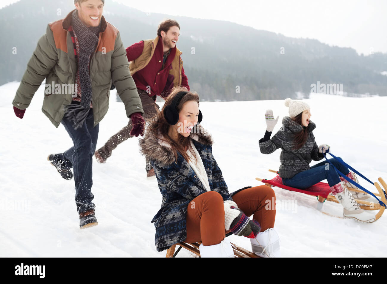 Enthusiastic friends sledding in snowy field Stock Photo - Alamy
