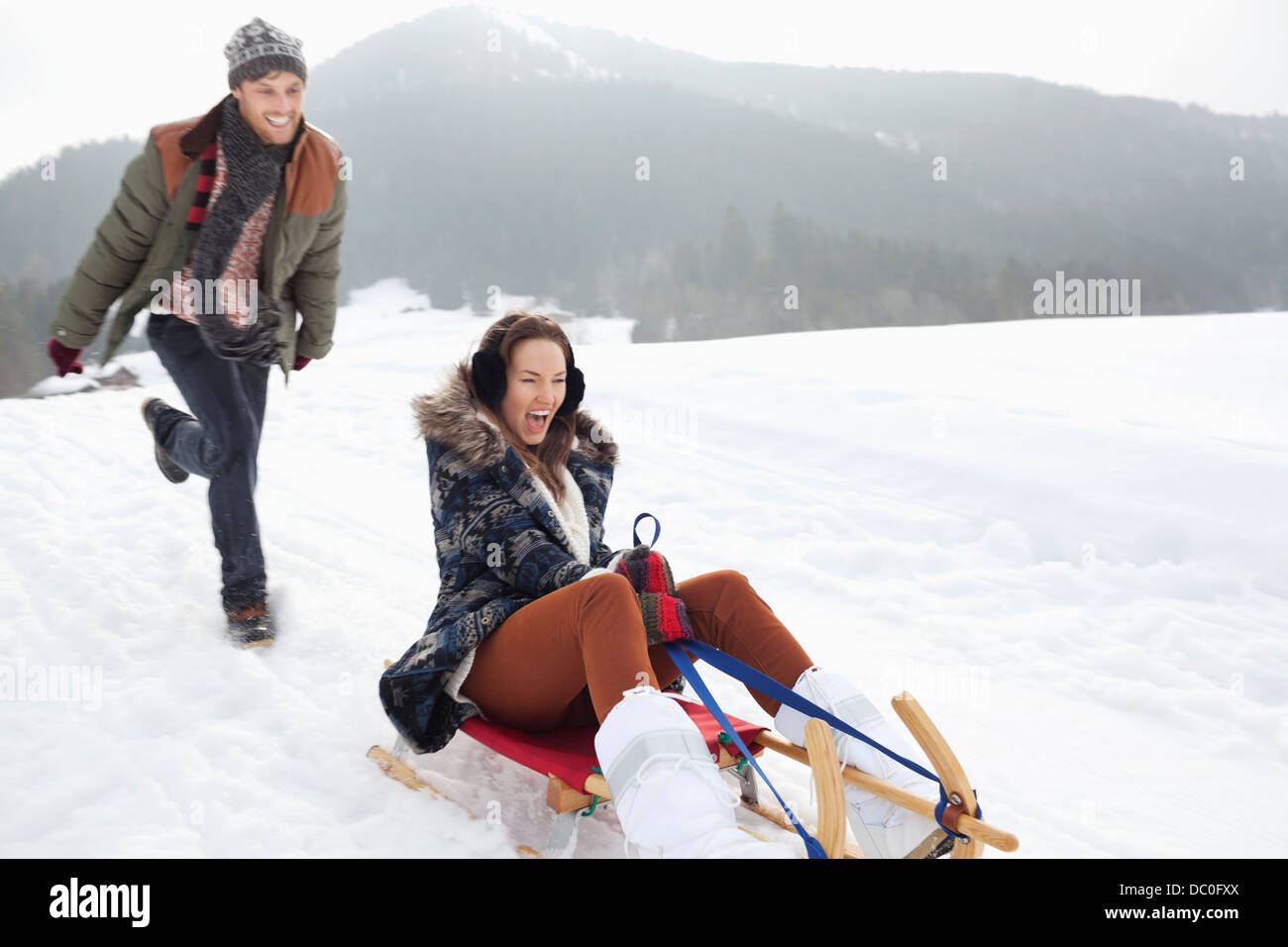 Enthusiastic couple sledding in snowy field Stock Photo - Alamy
