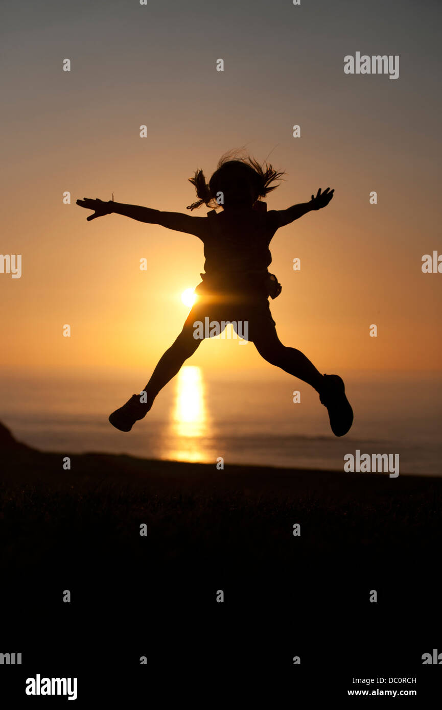 A young girl jumping and playing in front of a setting sun near St ...