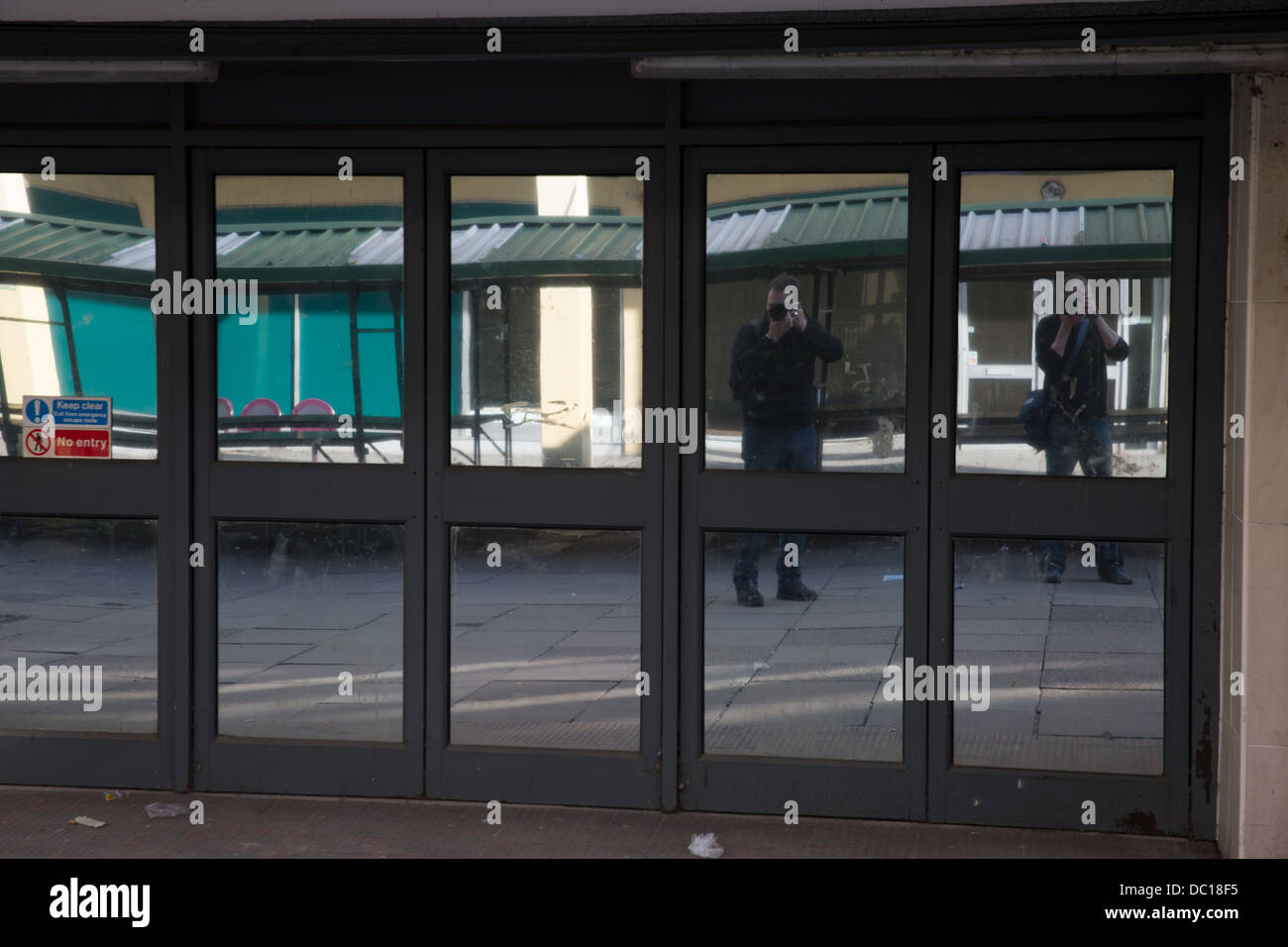 Two photographers take a photograph in a reflective street shop window ...