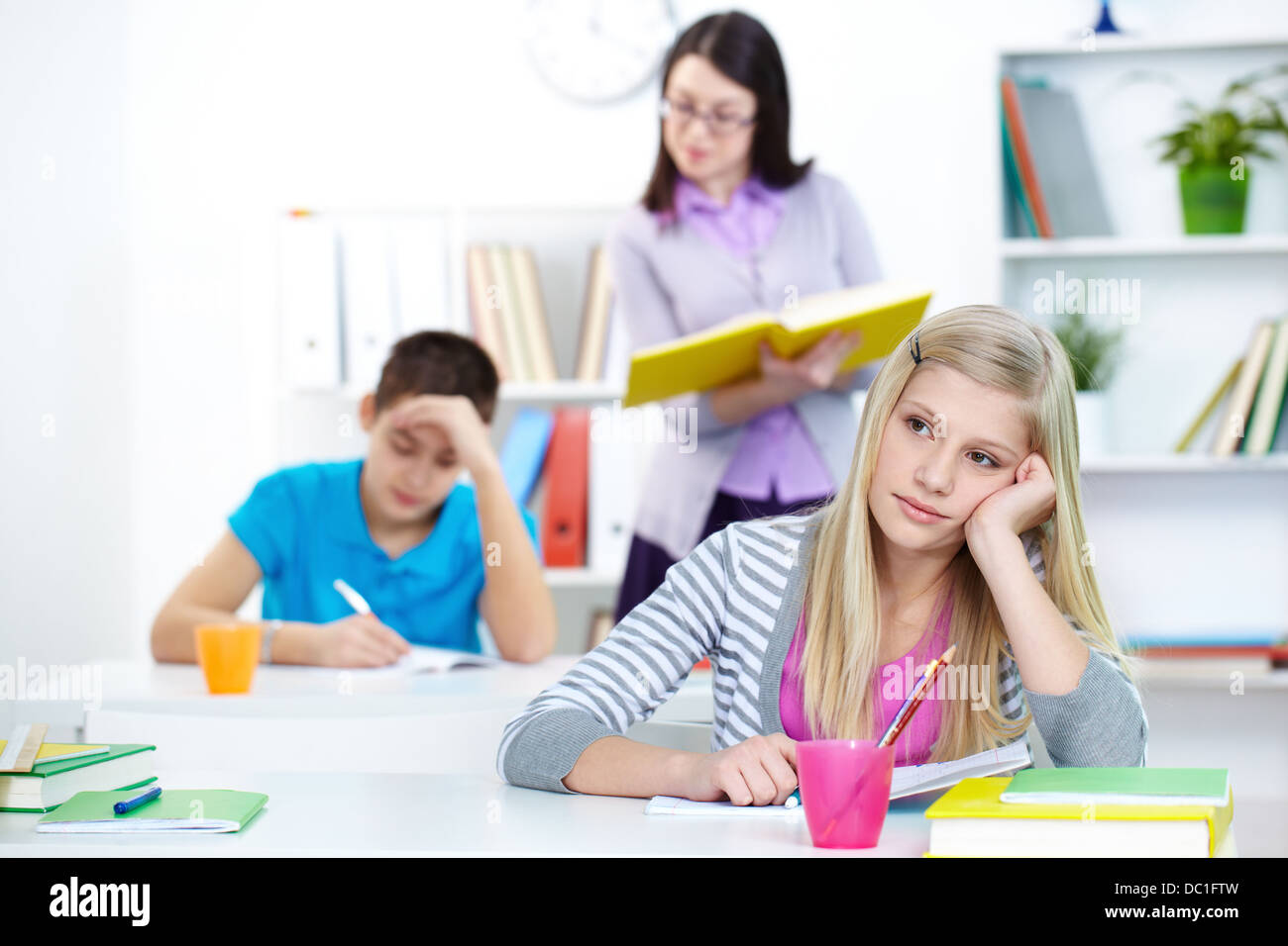 Portrait of bored teenage blonde sitting at lesson with teacher and ...