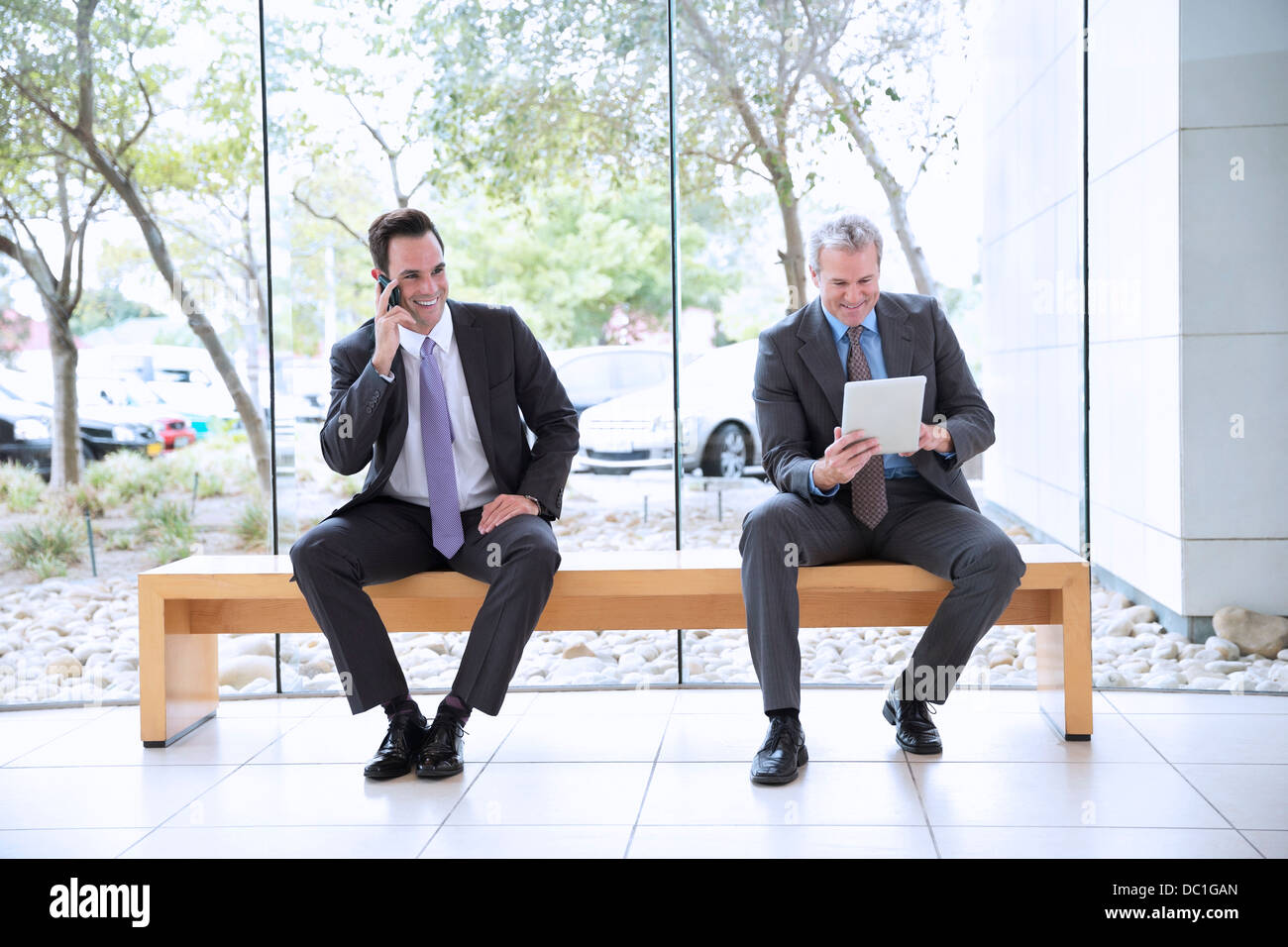 Businessmen using cell phone and digital tablet in lobby Stock Photo - Alamy