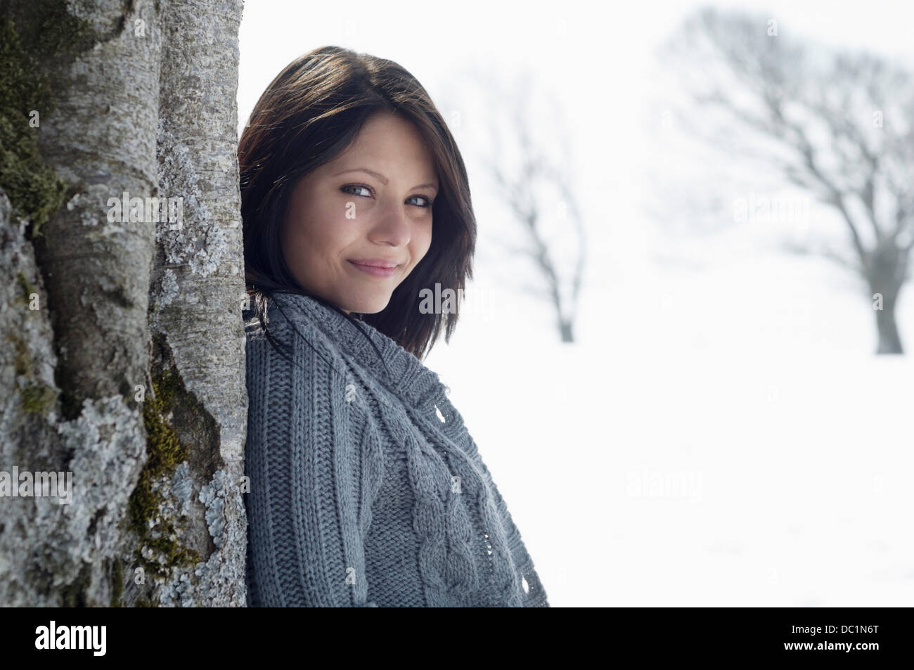Young female leaning against bare tree in snowy field Stock Photo - Alamy