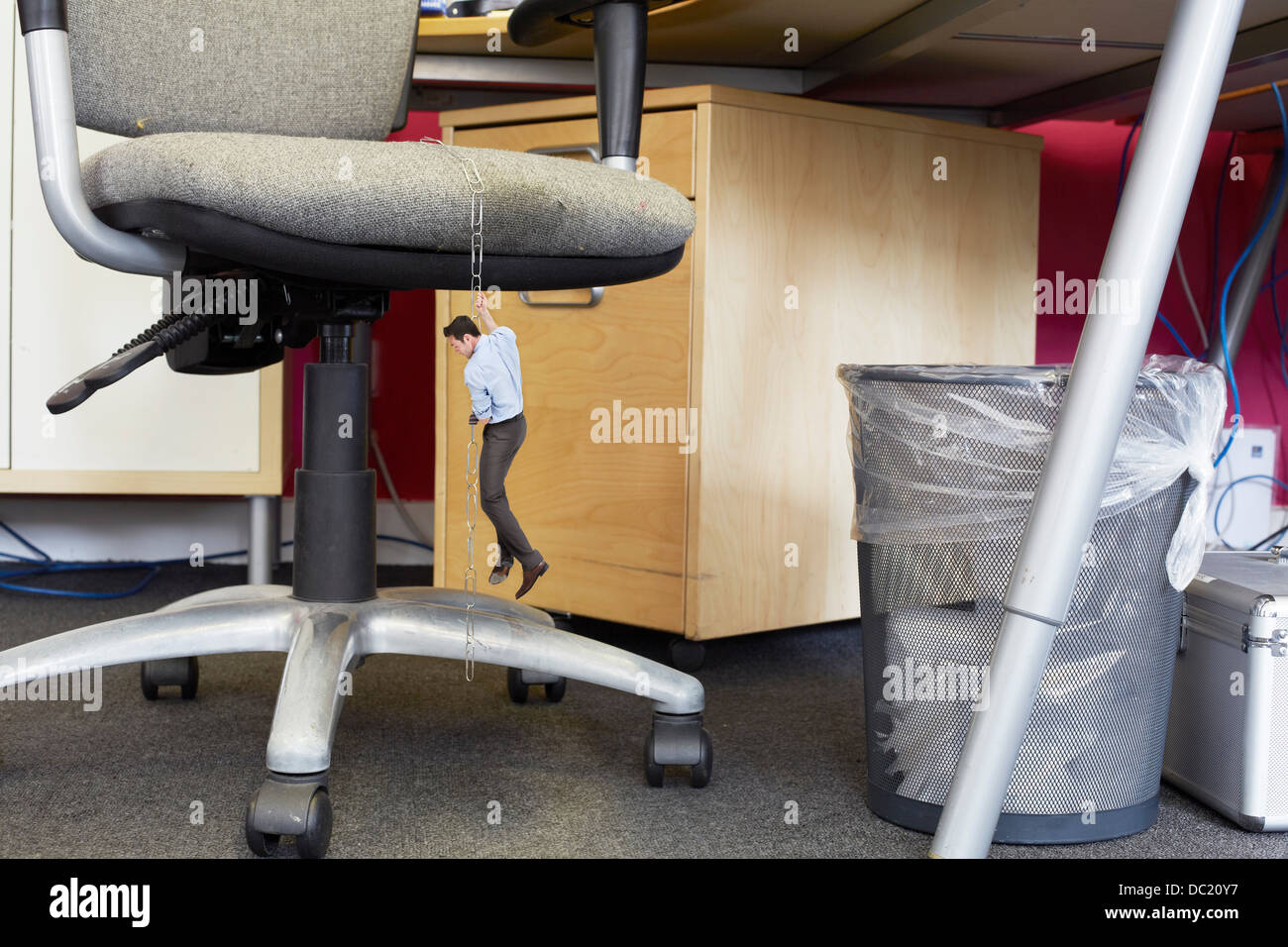 Businessman climbing down large paper clips on oversized office chair ...