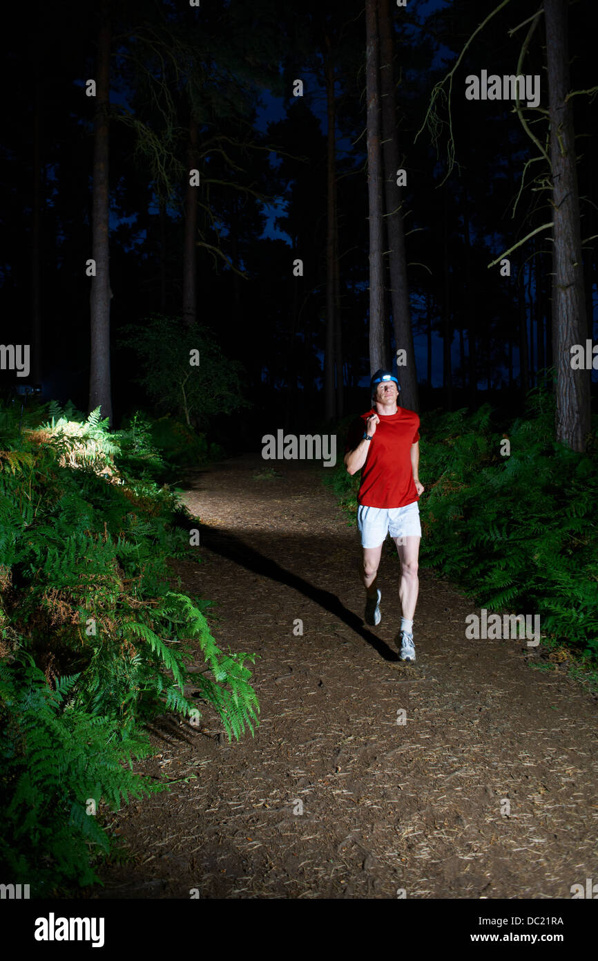 Mid adult man jogging through forest at night Stock Photo - Alamy