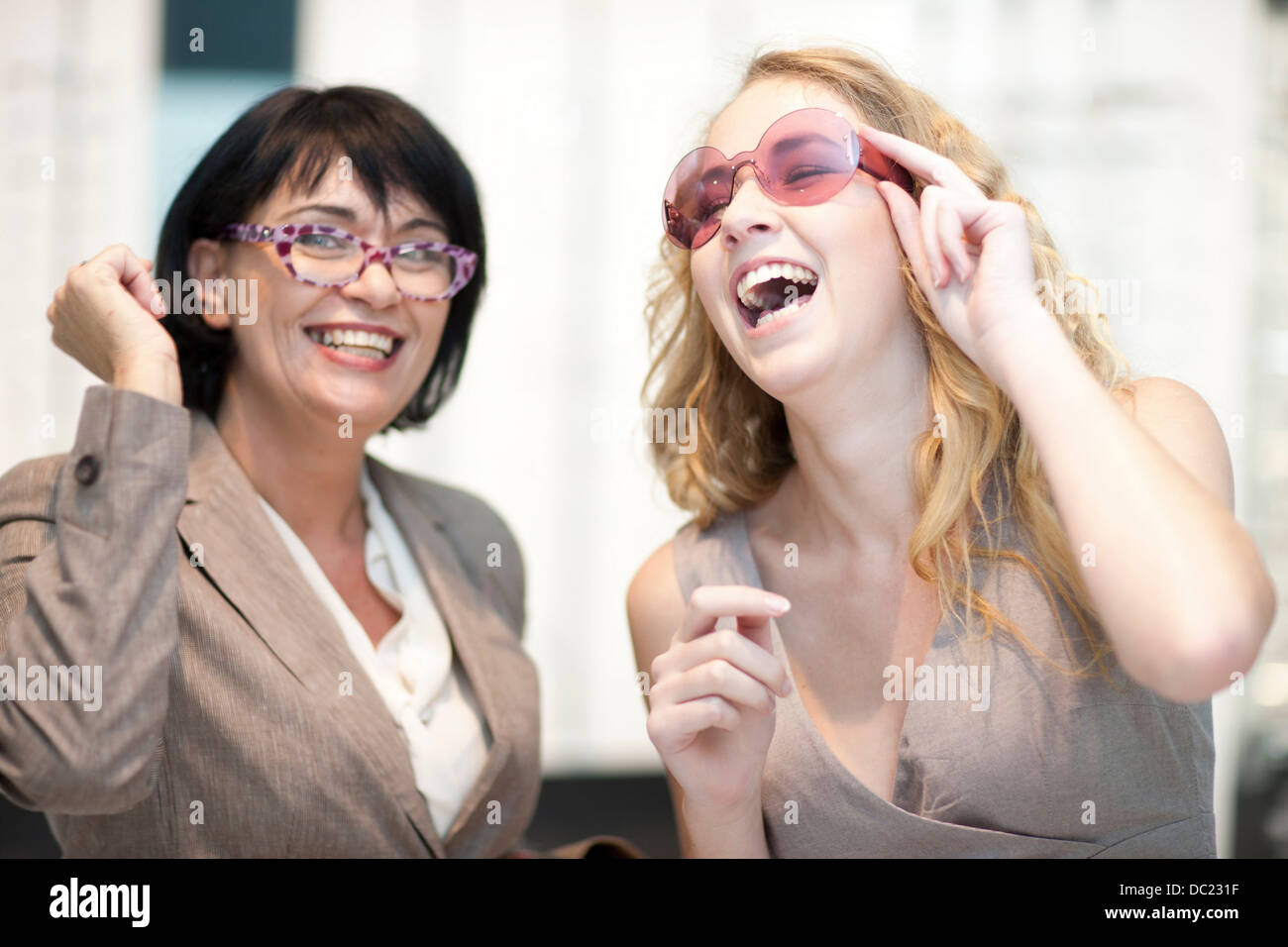 Two women laughing whilst trying on eyeglasses Stock Photo - Alamy