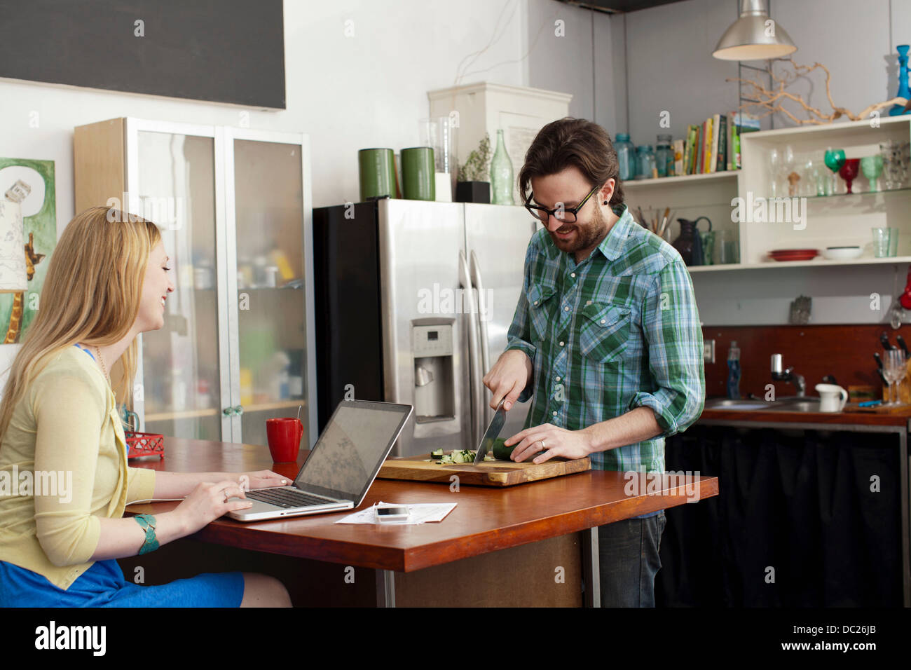 Woman on laptop computer, man chopping vegetables Stock Photo - Alamy