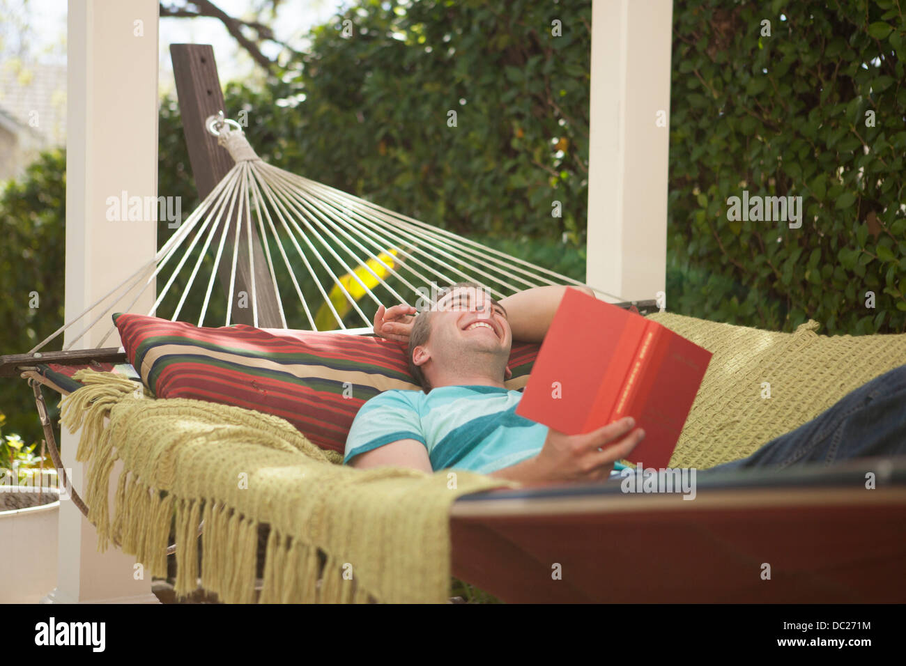 Young man reading book in hammock, laughing Stock Photo - Alamy