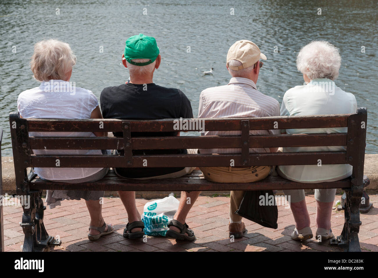 Rear view of elderly people sitting on a bench overlooking a river on a ...