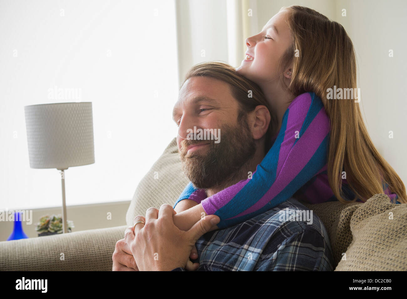 Daughter hugging father from behind sofa Stock Photo - Alamy