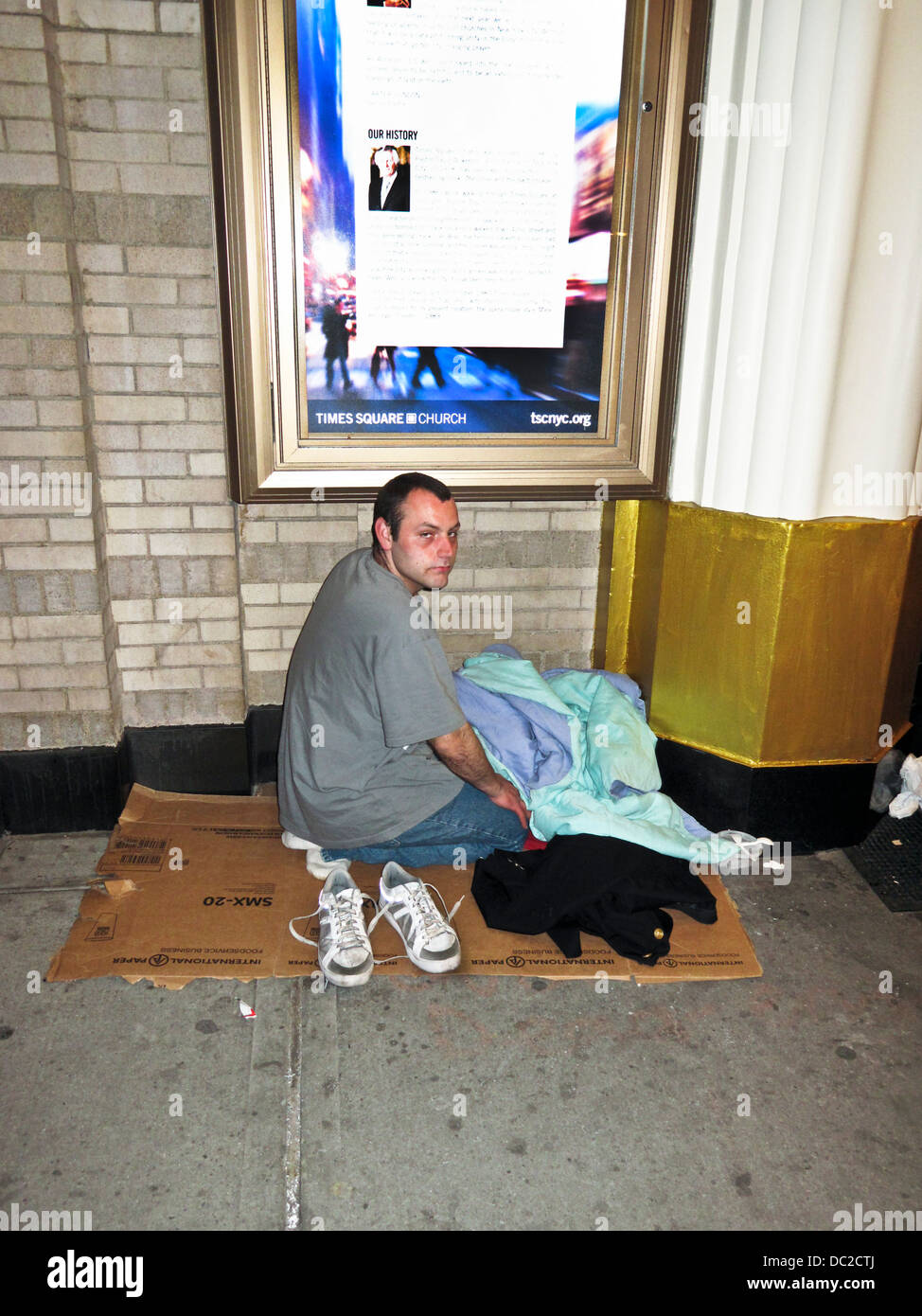 young clean shaven homeless man prepares his bed on sidewalk outside ...