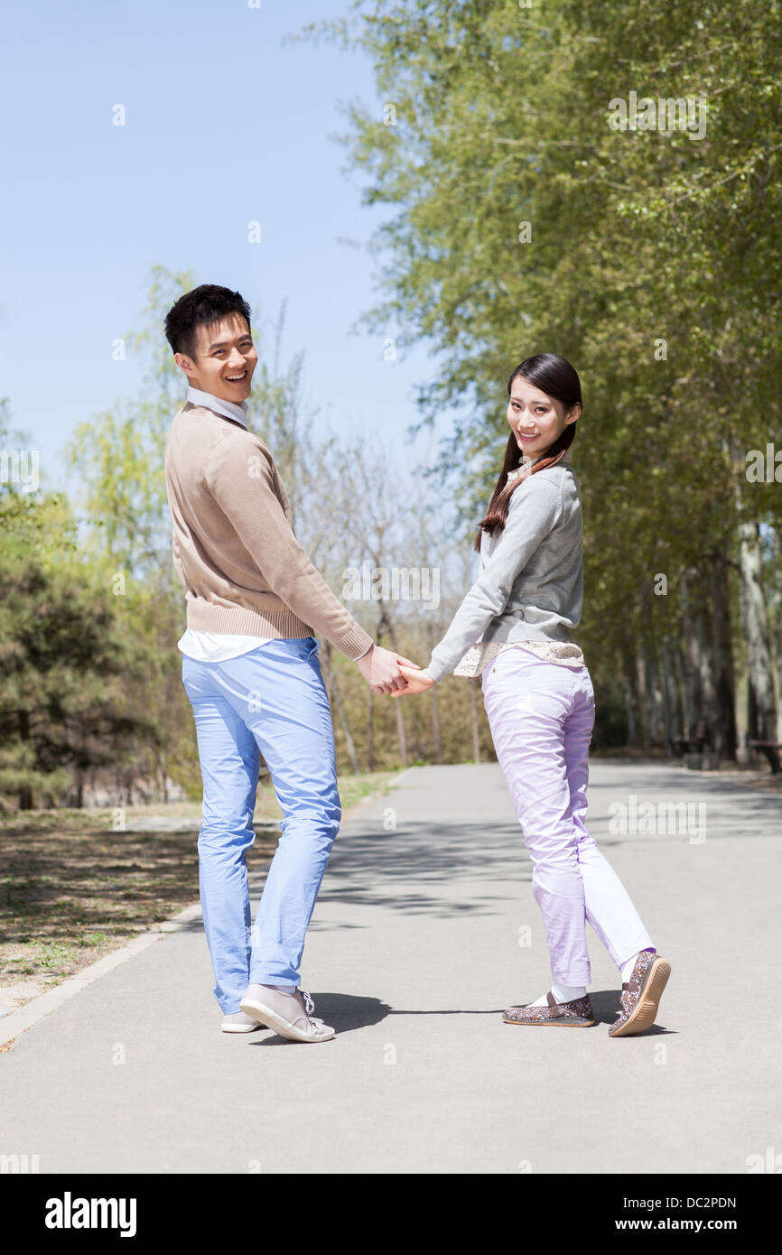 Happy young couple looking over shoulders hand in hand Stock Photo - Alamy