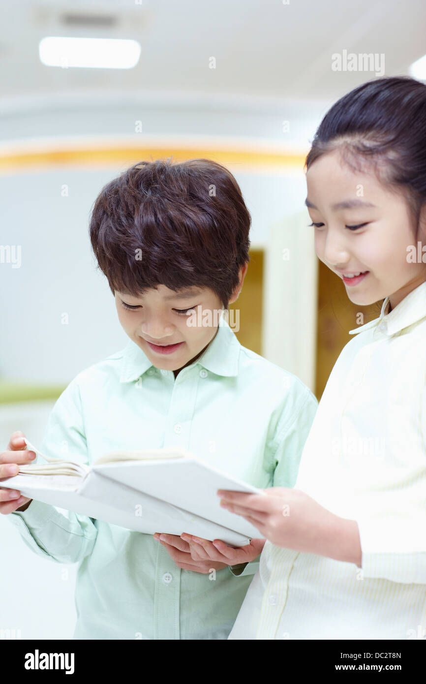 a girl and a boy reading a book while standing Stock Photo - Alamy