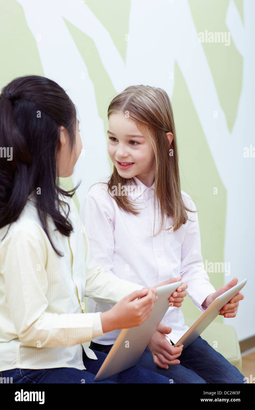 two girls sitting on a chair with tablet PC Stock Photo - Alamy