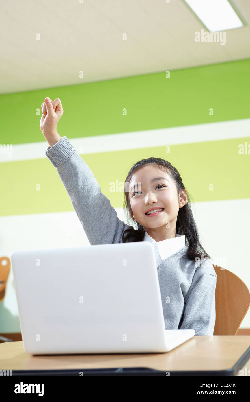 a girl raising her hand while using a laptop in a classroom Stock Photo ...