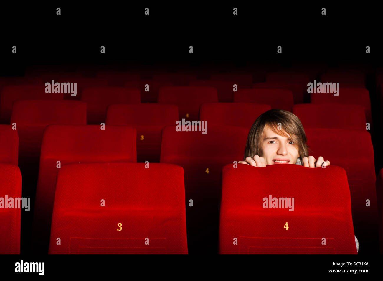 young man in the cinema hiding behind a chair Stock Photo - Alamy