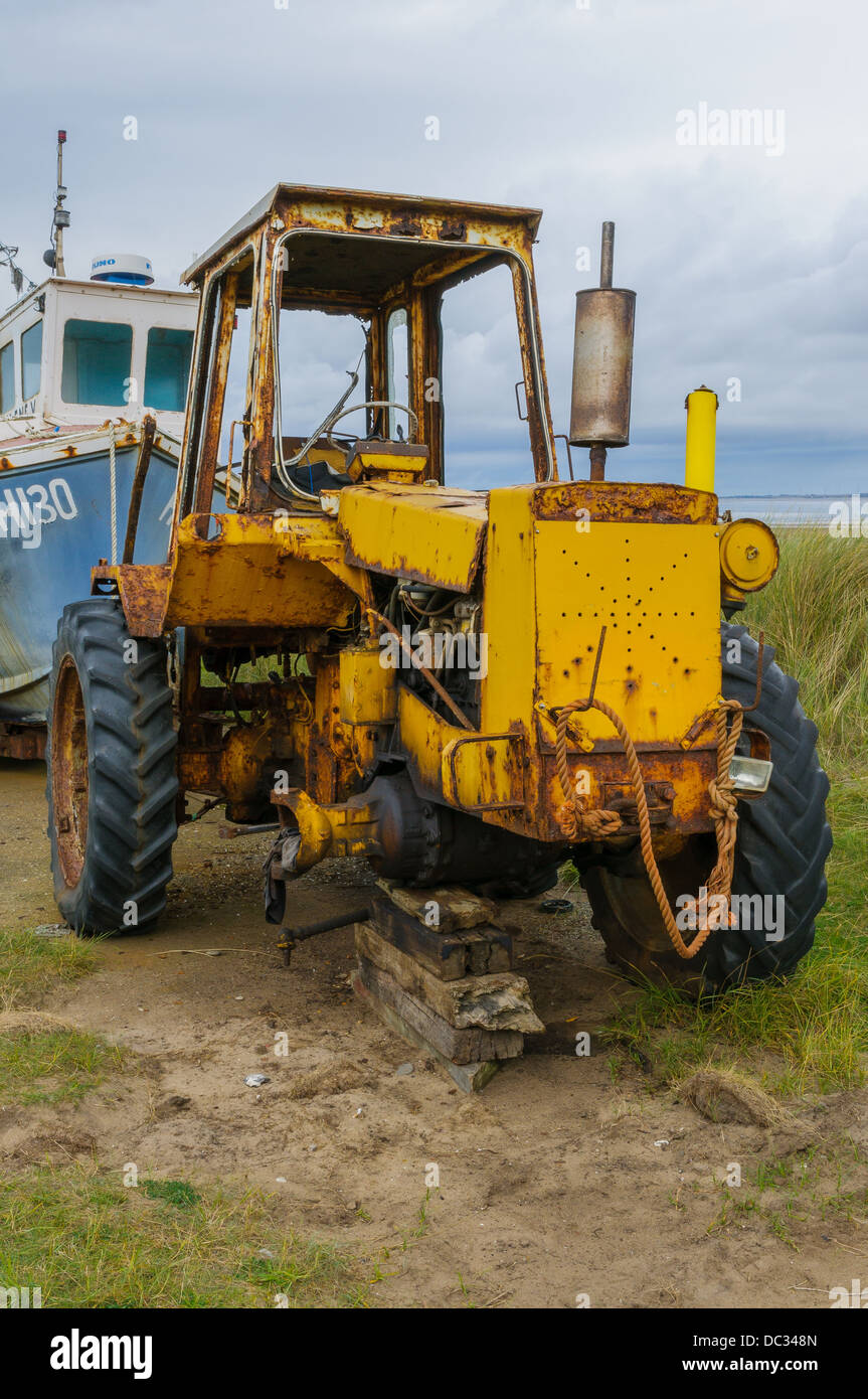A disused rusted, yellow tractor missing a front wheel. It was used to ...