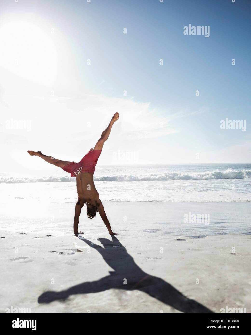 Man in swim trunks doing handstand on beach Stock Photo - Alamy