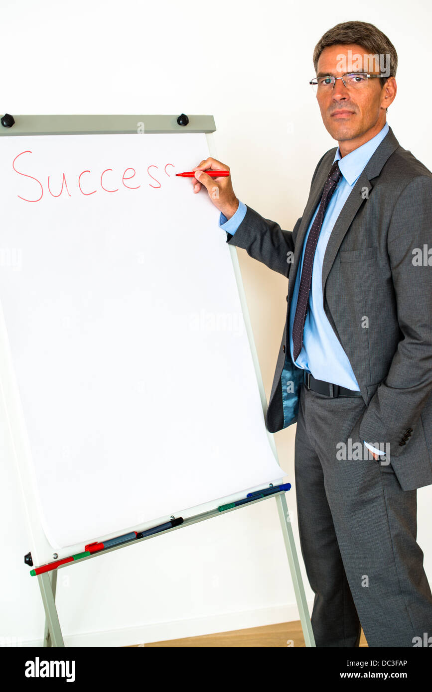 Portrait of a businessman writing success in red letters on flipchart ...