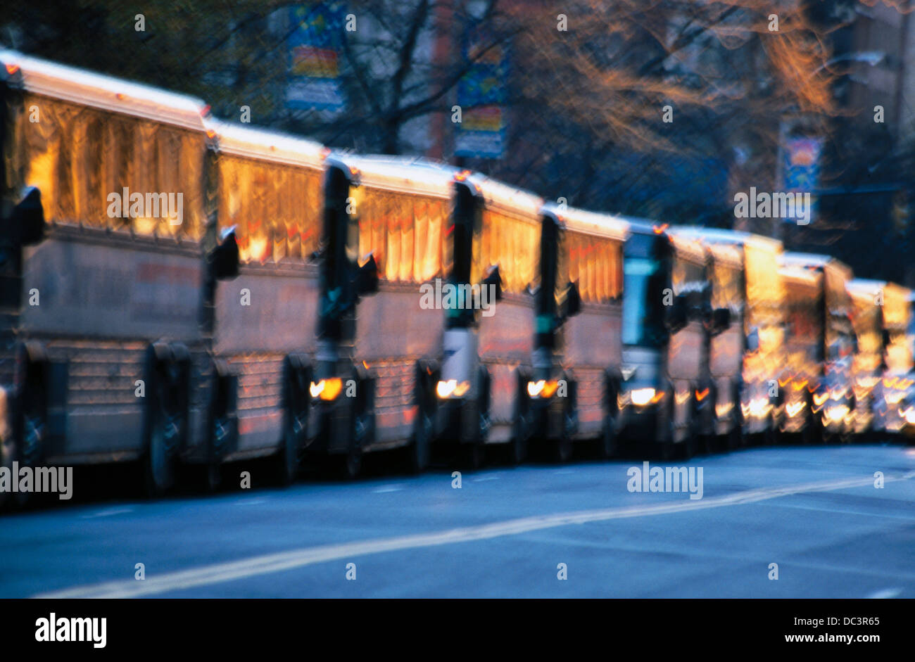 A line of tour buses parked on a city street in early morning light ...