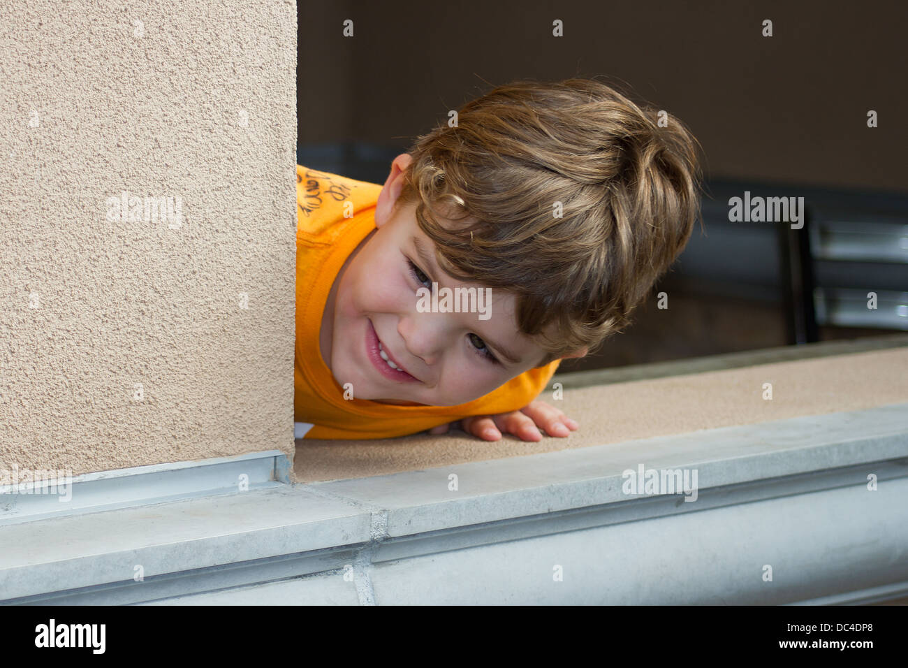 A young Caucasian boy with cute smile leaning out a window Stock Photo ...