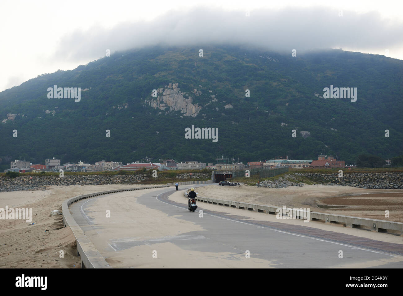 A lone scooter rider commuting on the sand blown roads of Beigan Island ...