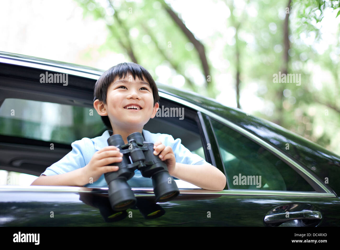 Cheerful boy leaning out of car window with binoculars in hands Stock ...