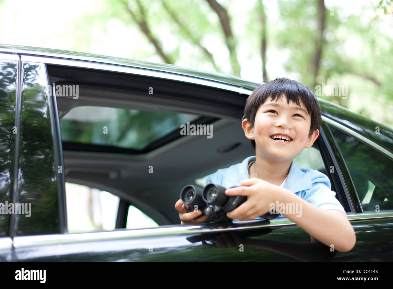 Cheerful boy leaning out of car window with binoculars in hands Stock ...