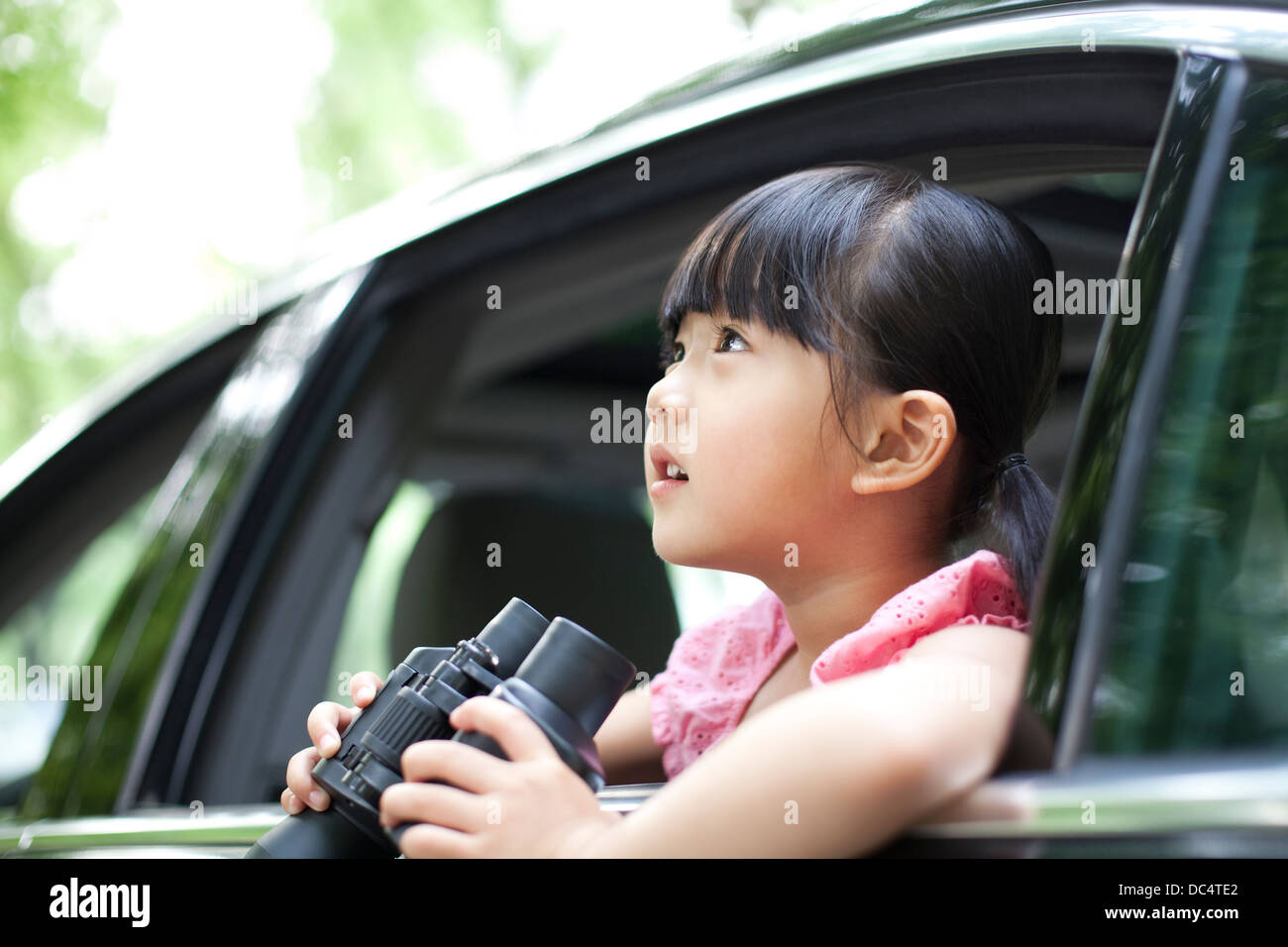 Cute girl leaning out of car window with binoculars in hands Stock ...
