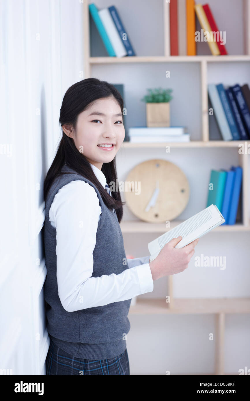 student in school uniform reading a book in front of bookshelf Stock ...