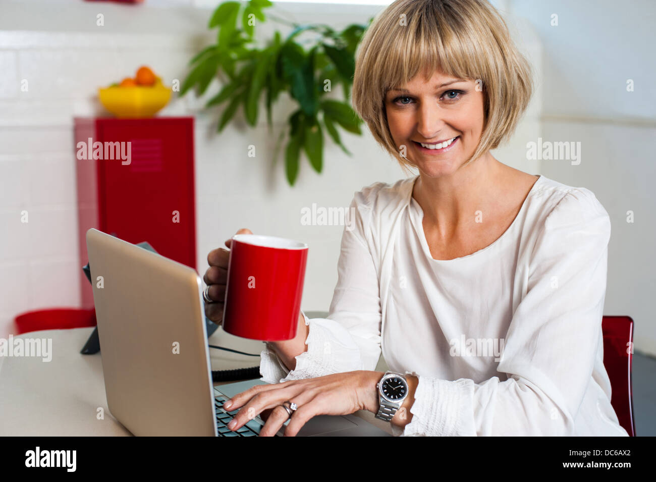 Cheerful woman holding coffee mug and working Stock Photo - Alamy