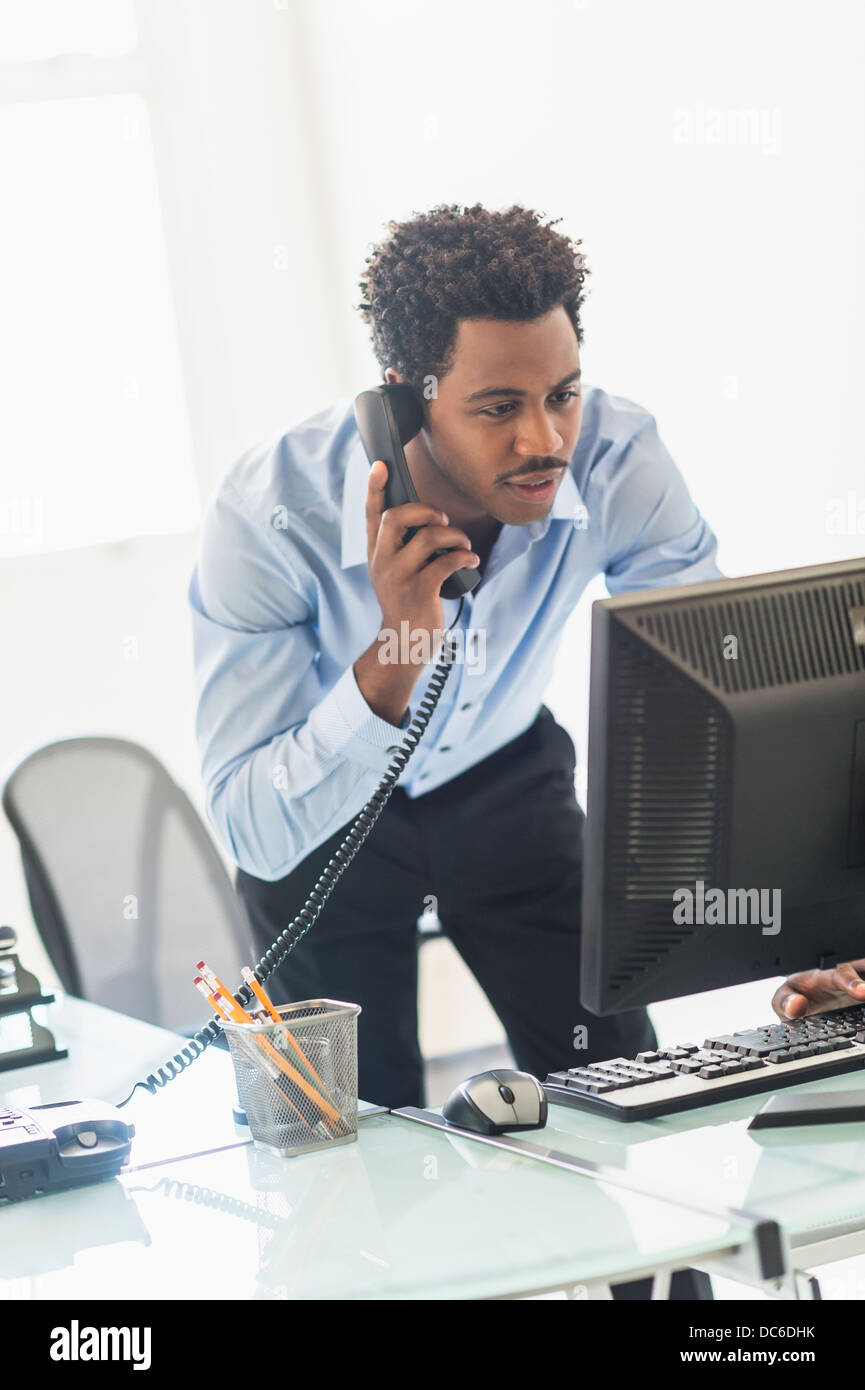 Businessman working on computer and talking on cell phone Stock Photo ...