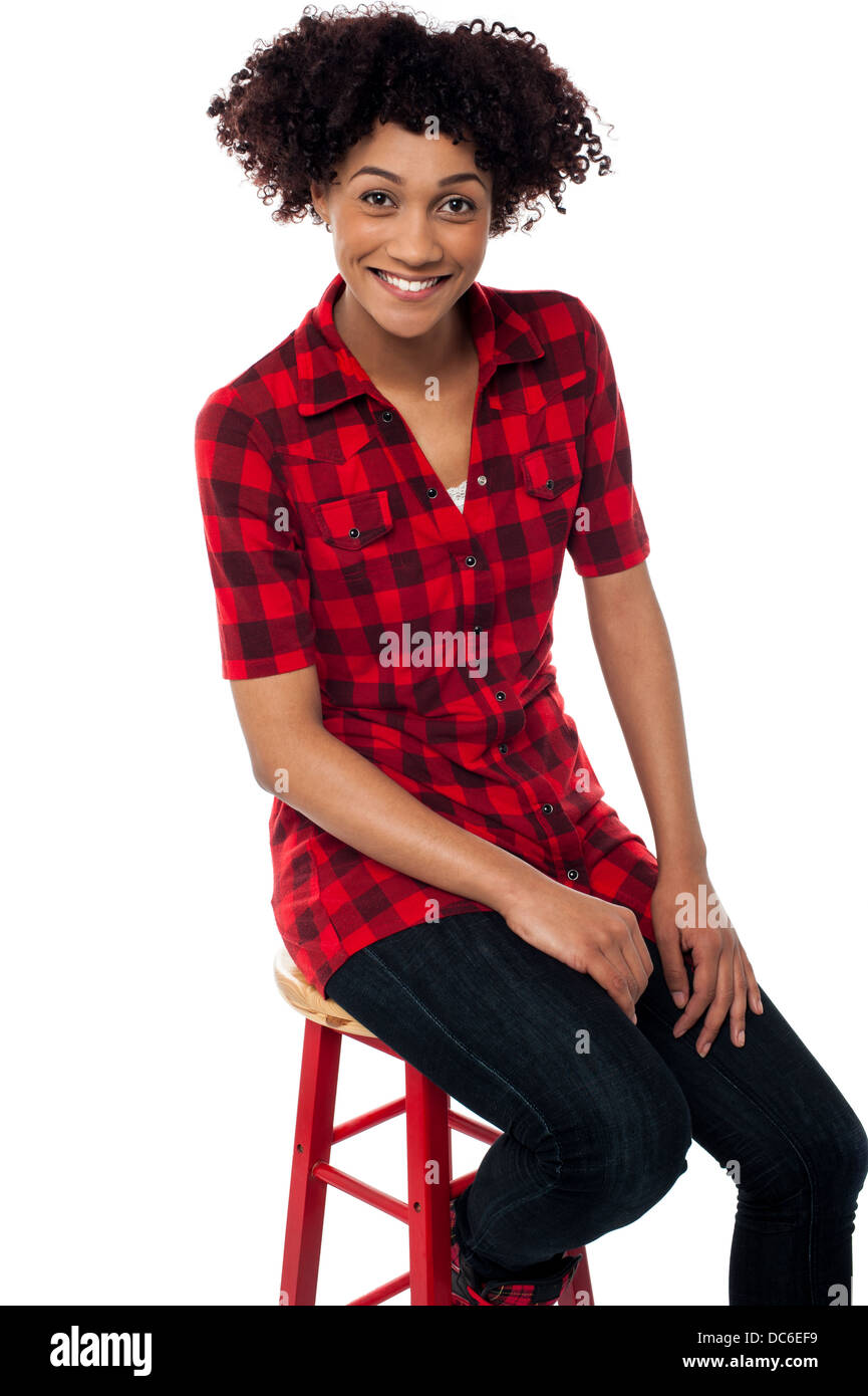 Curly haired fashion model sitting on red stool Stock Photo - Alamy
