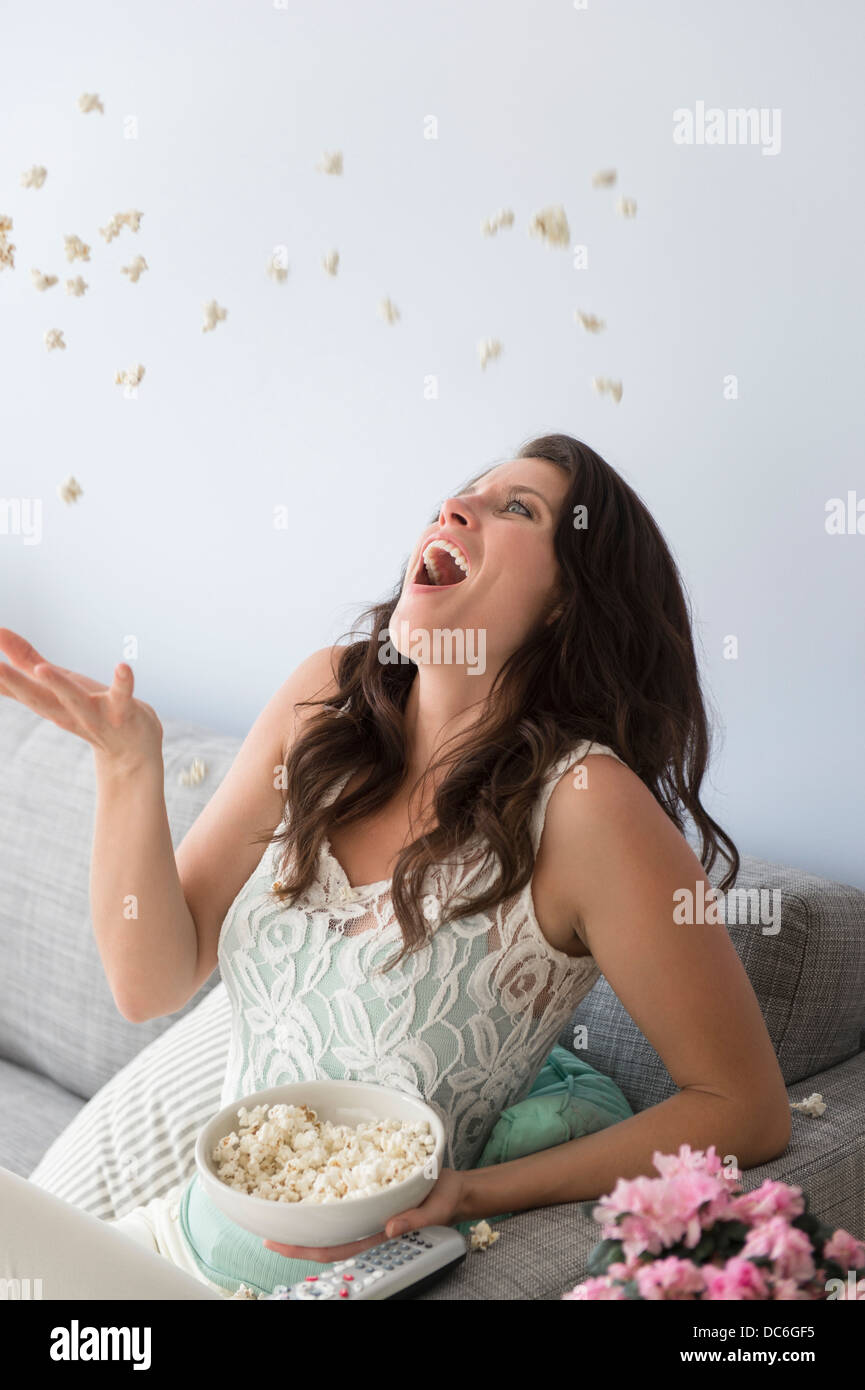 Young woman on sofa, throwing and catching popcorn Stock Photo - Alamy