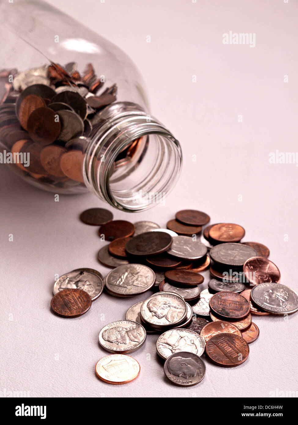 American coins are spilling out from a tipped over jar onto a white ...