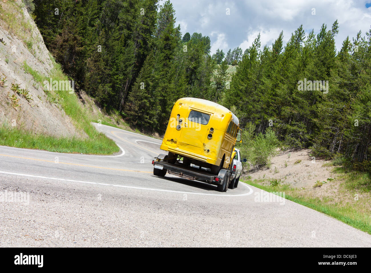 A truck pulling a yellow school bus rounds the curve on a highway in ...