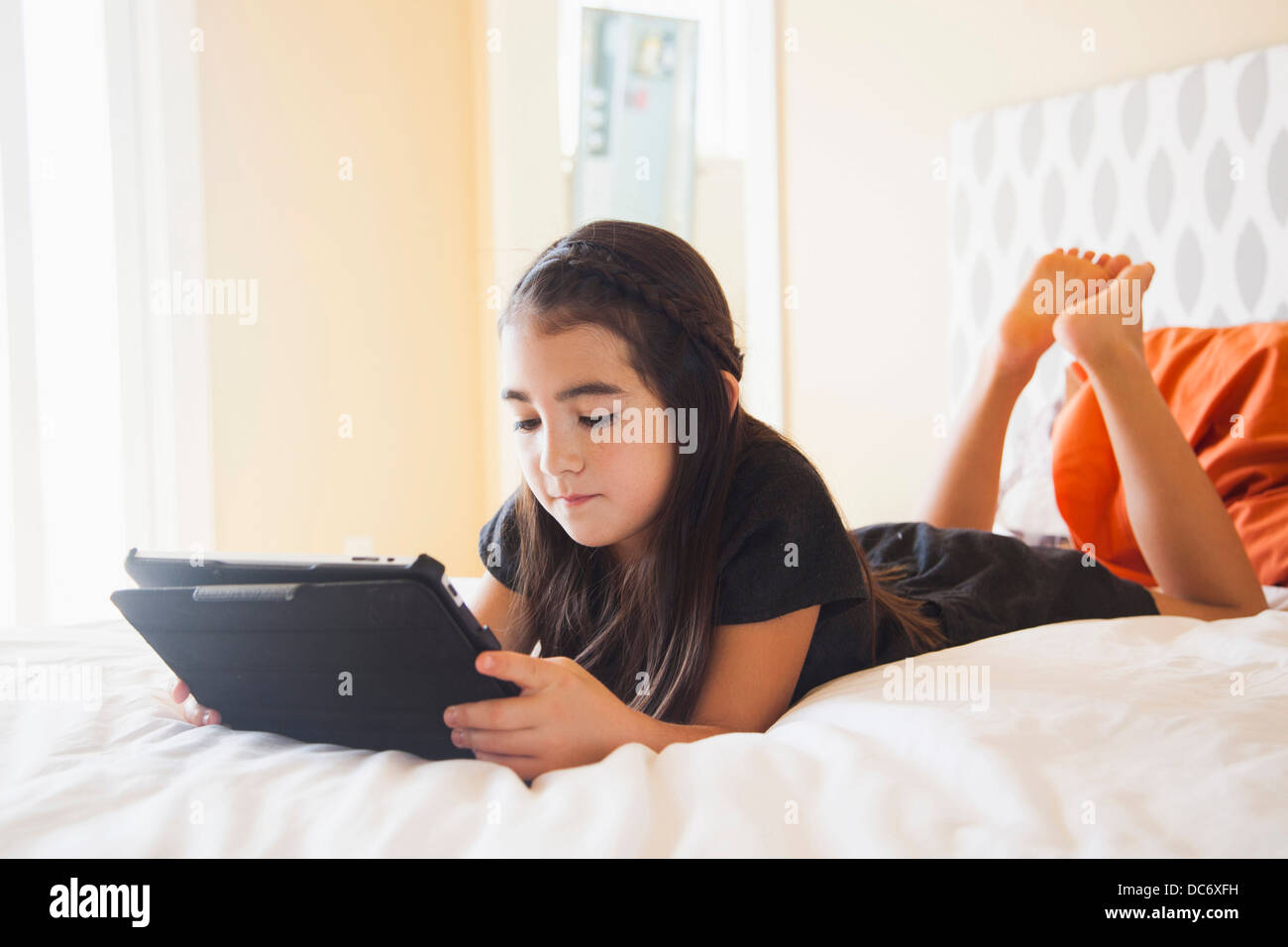 Girl (8-9) laying on bed and using digital tablet Stock Photo - Alamy