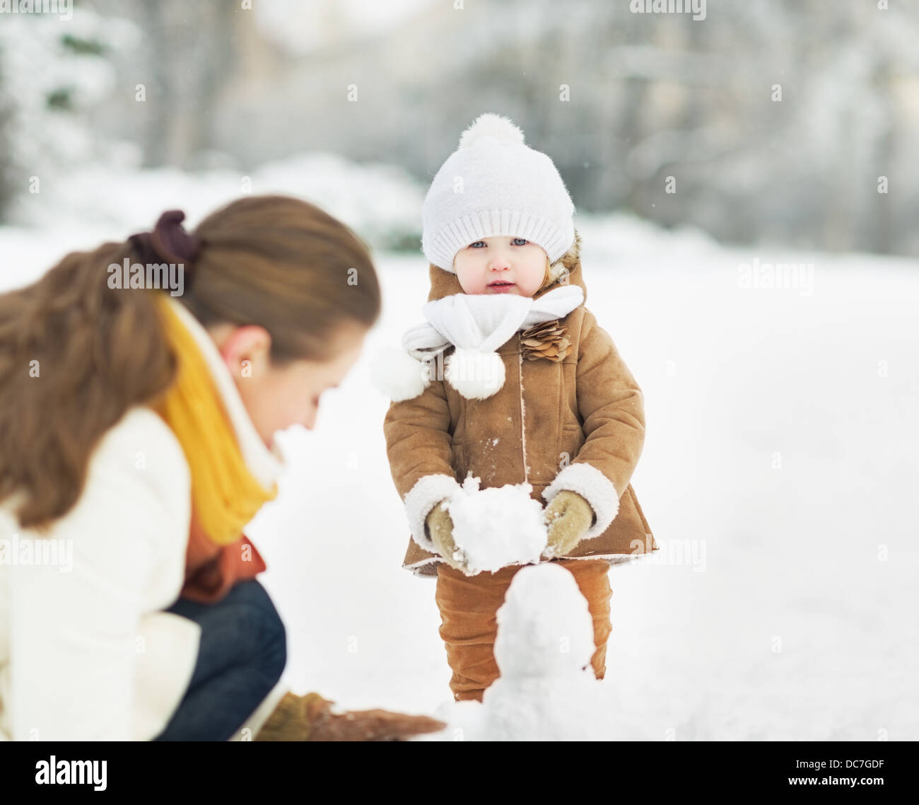 Happy mother and baby making snowman in winter park Stock Photo - Alamy