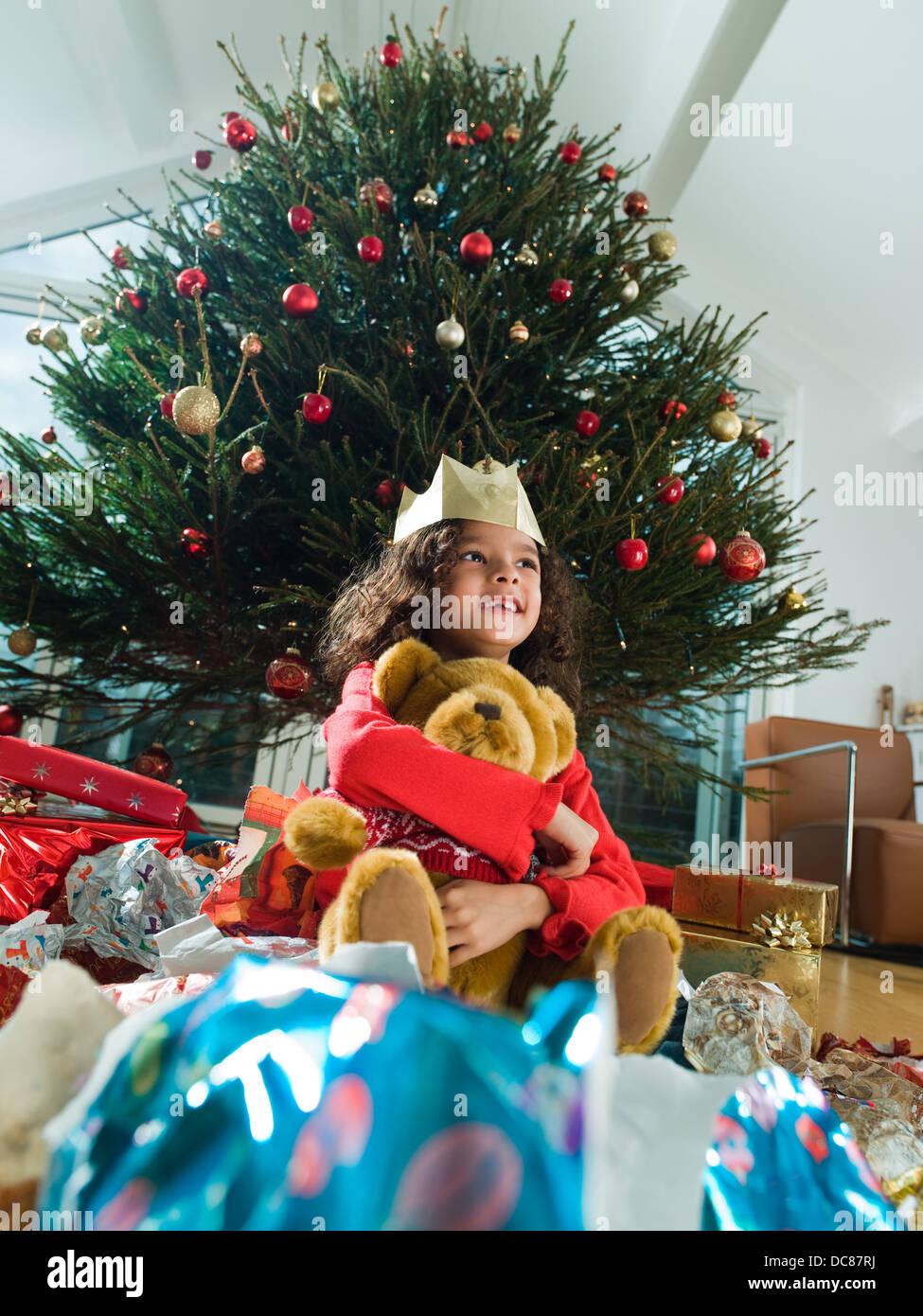 young girl holding teddy under christmas tree sitting in wrapping paper ...