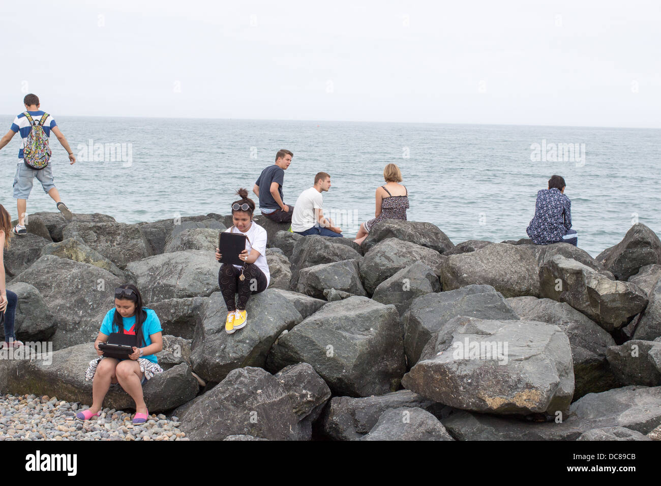 People sitting on the rocks at the beach in Bray Stock Photo - Alamy